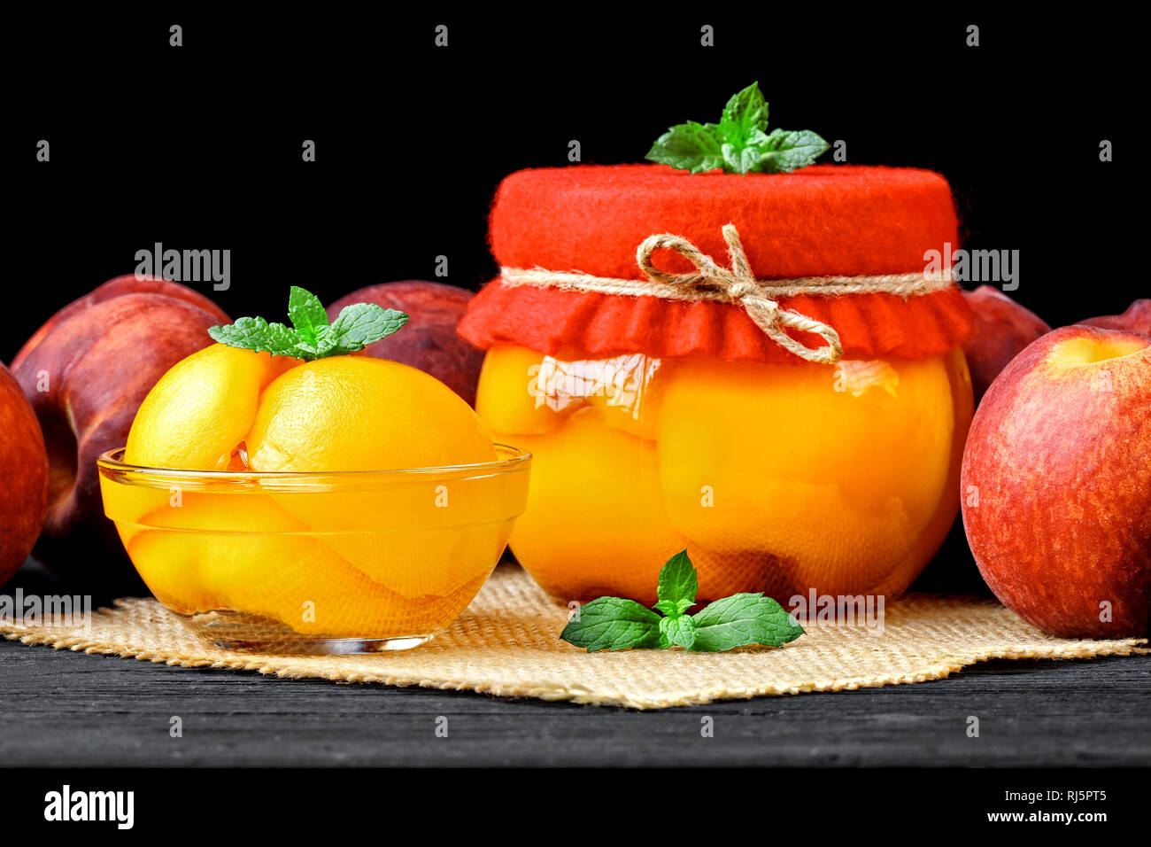 Peach compote with half peaches in glass jars on an old black wooden ...