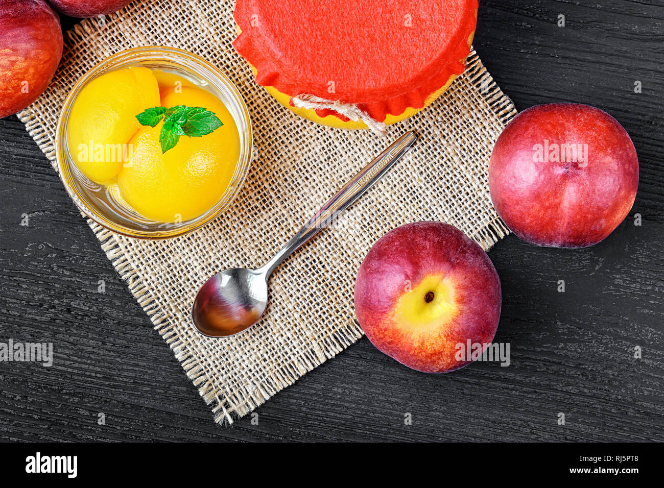 Peach compote with half peaches in glass jars on an old black wooden ...