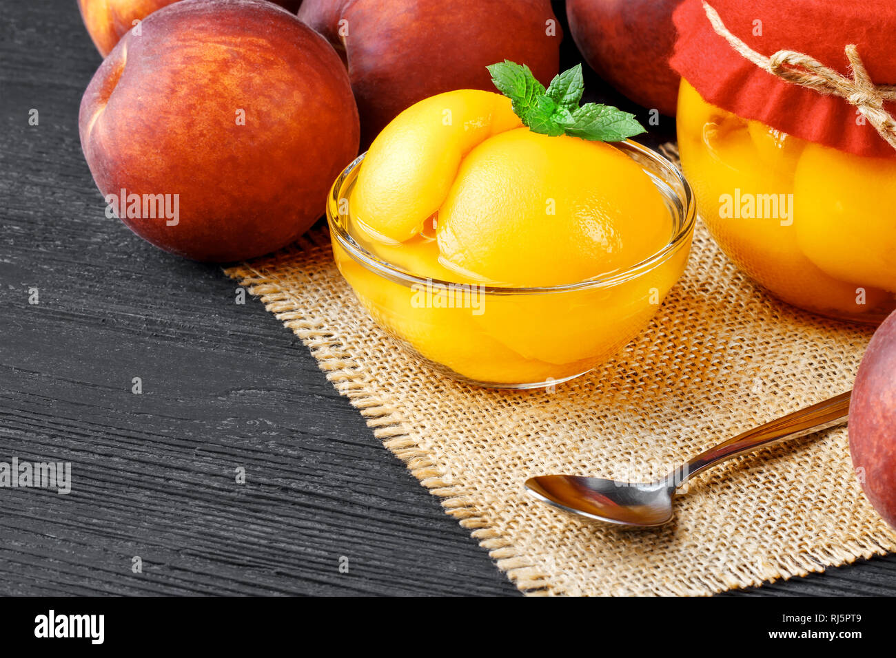 Peach compote with half peaches in glass jars on an old black wooden ...