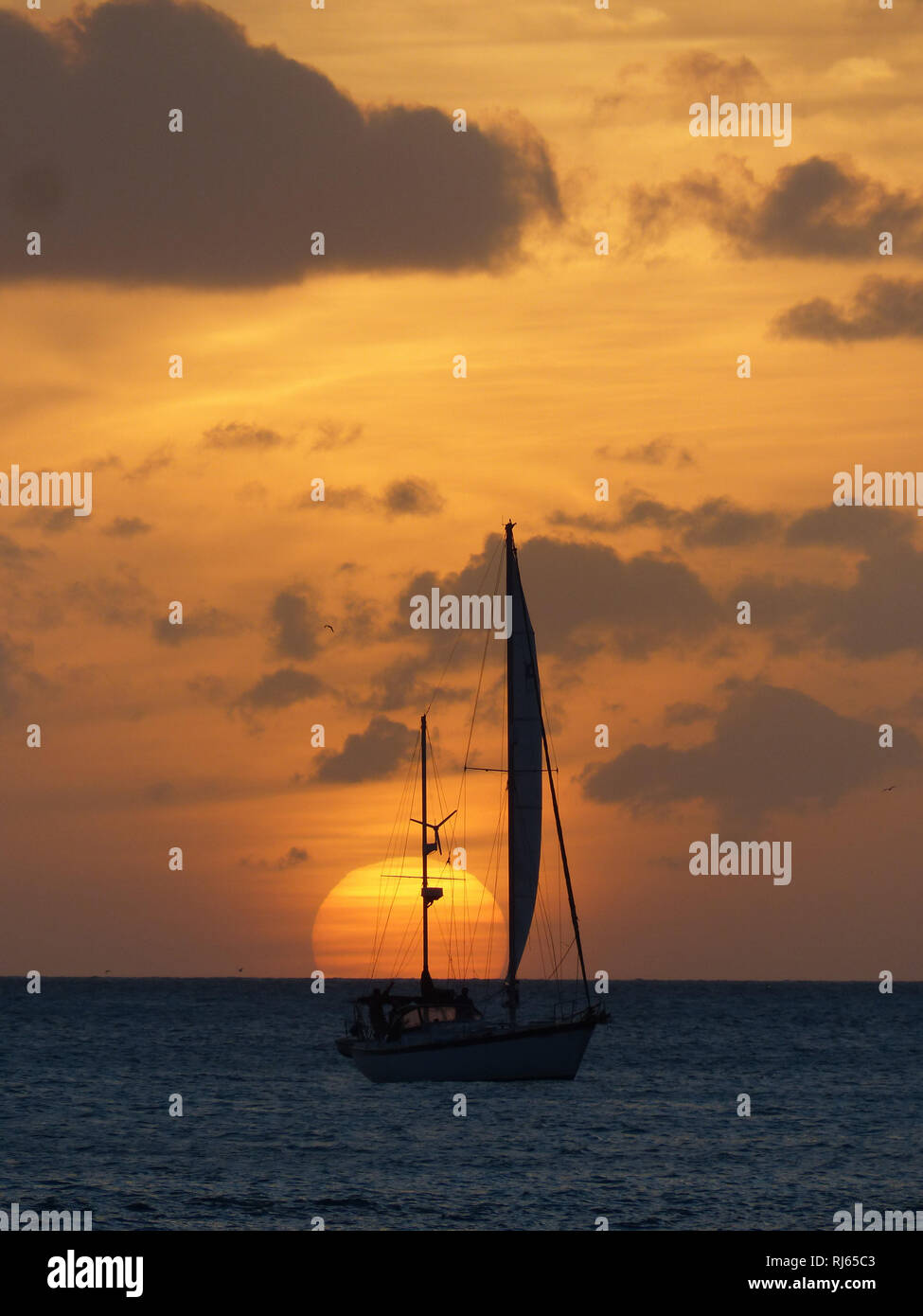 Sail boat in the distance at sea with setting sun Stock Photo - Alamy