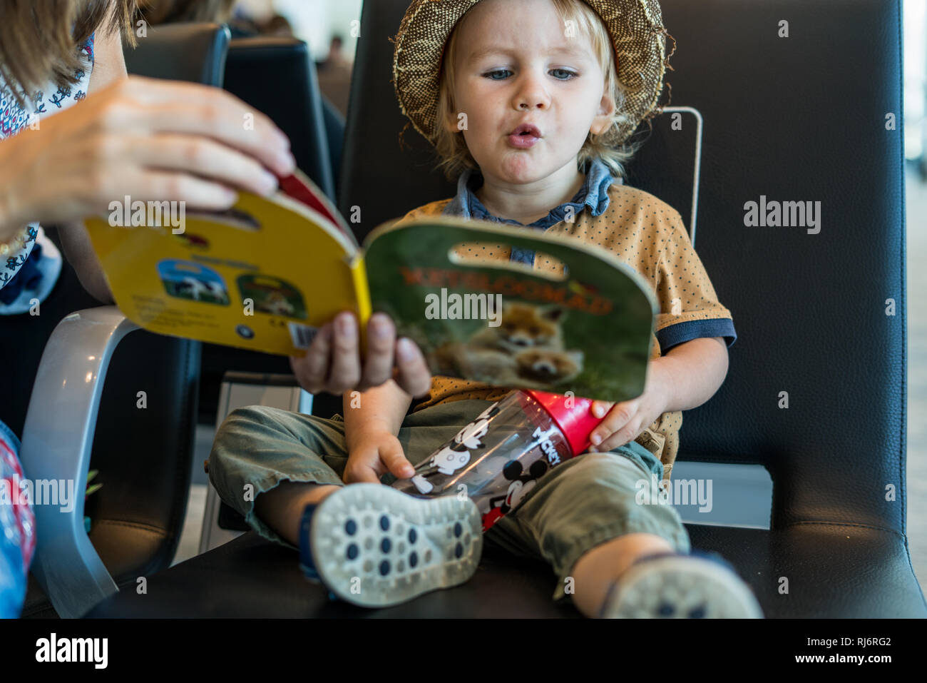 A portrait of a young studious baby boy reading a book with his mother ...