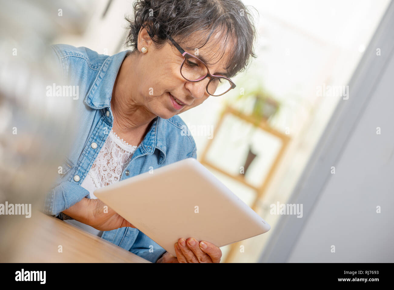 charming senior brunette woman with glasses using a digital tablet at ...