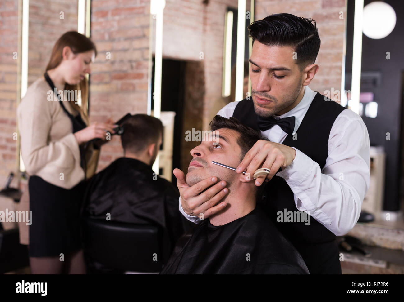 Male client getting old-fashioned shave with straight razor from male ...