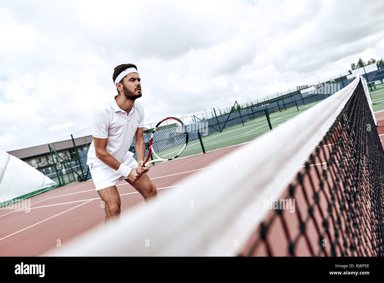 Handsome man holding tennis racket and looking concentrated while ...