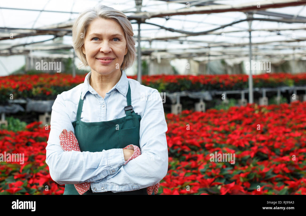 Confident middle-aged female standing in her greenhouse on background ...