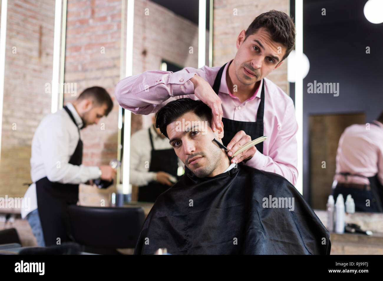 Handsome young man during beard shaving by professional barber in ...