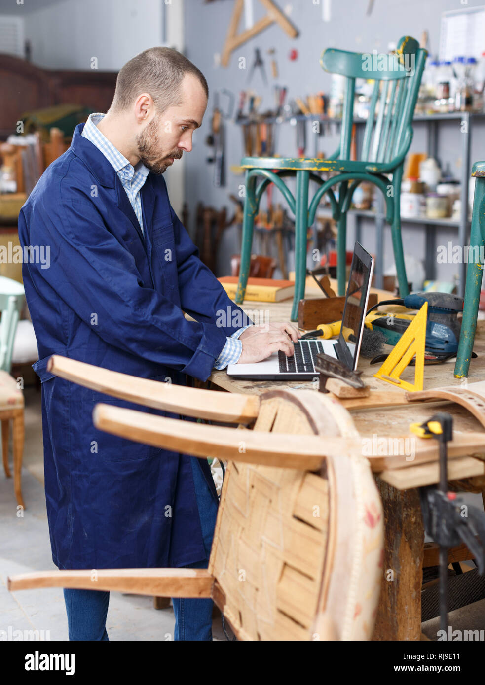 Furniture restorer using laptop in process of renovation vintage chair ...