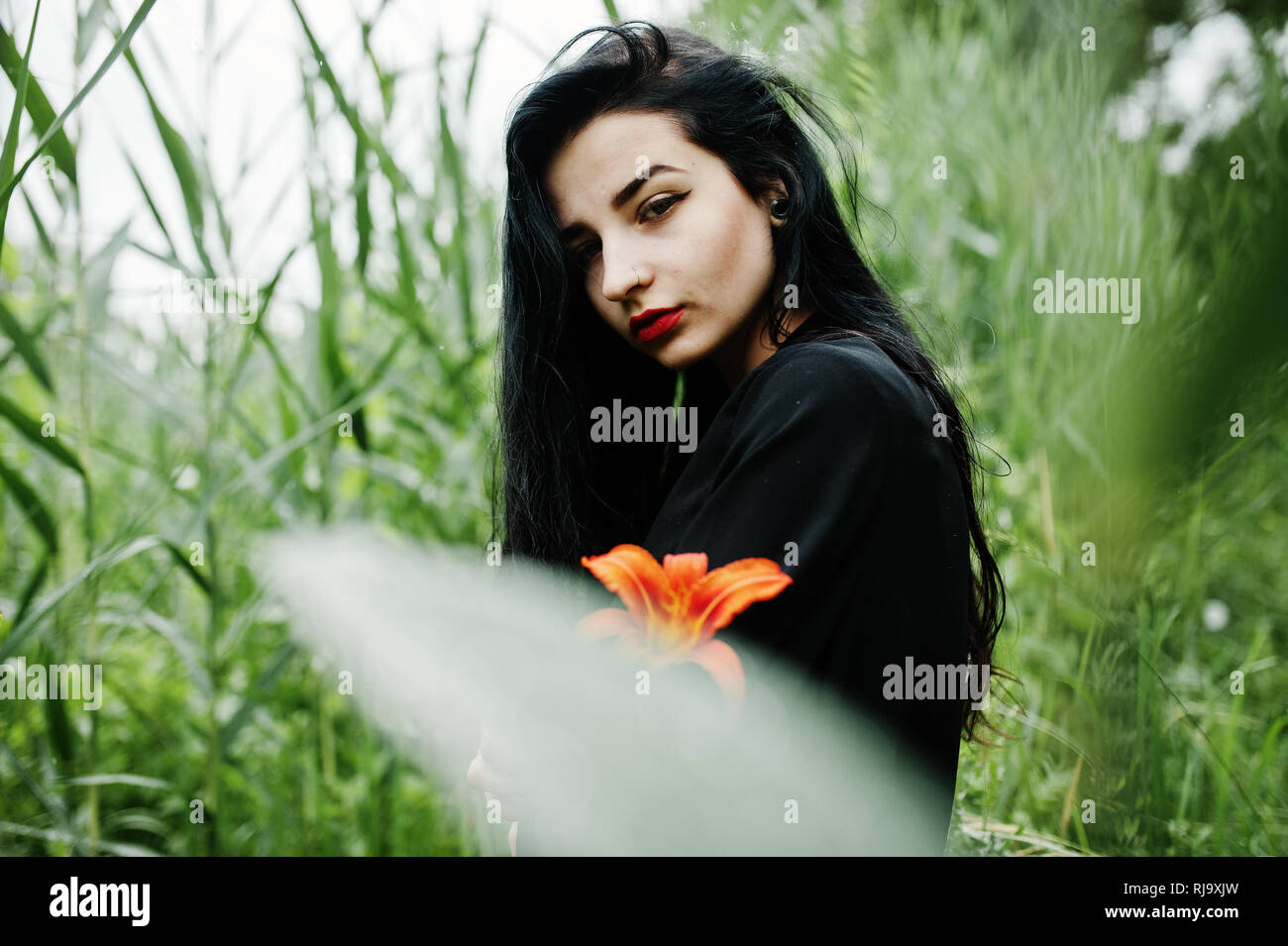 Sensual girl all in black, red lips. Goth dramatic woman hold orange ...