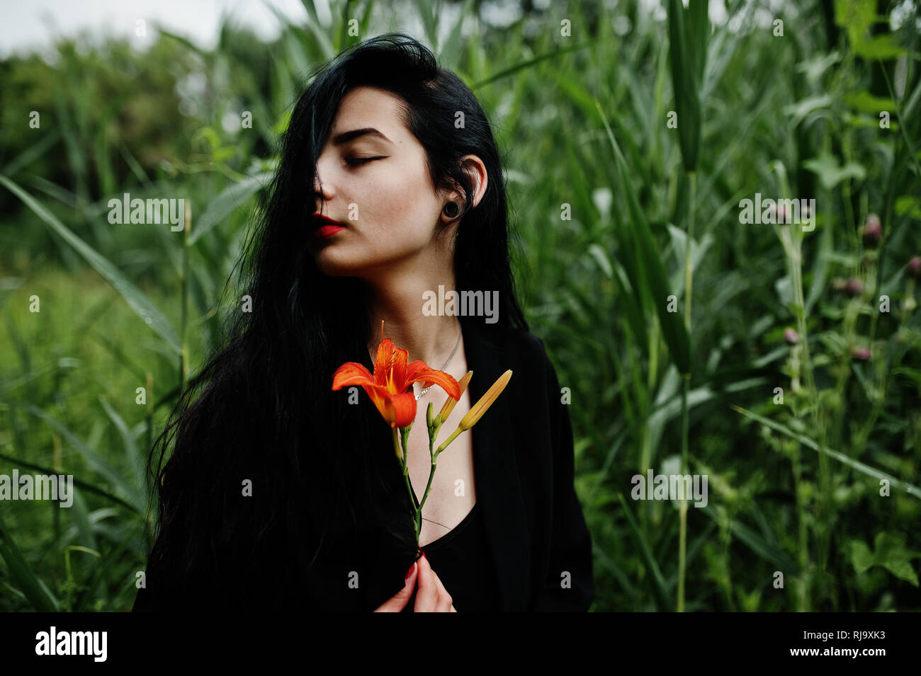 Sensual girl all in black, red lips. Goth dramatic woman hold orange ...