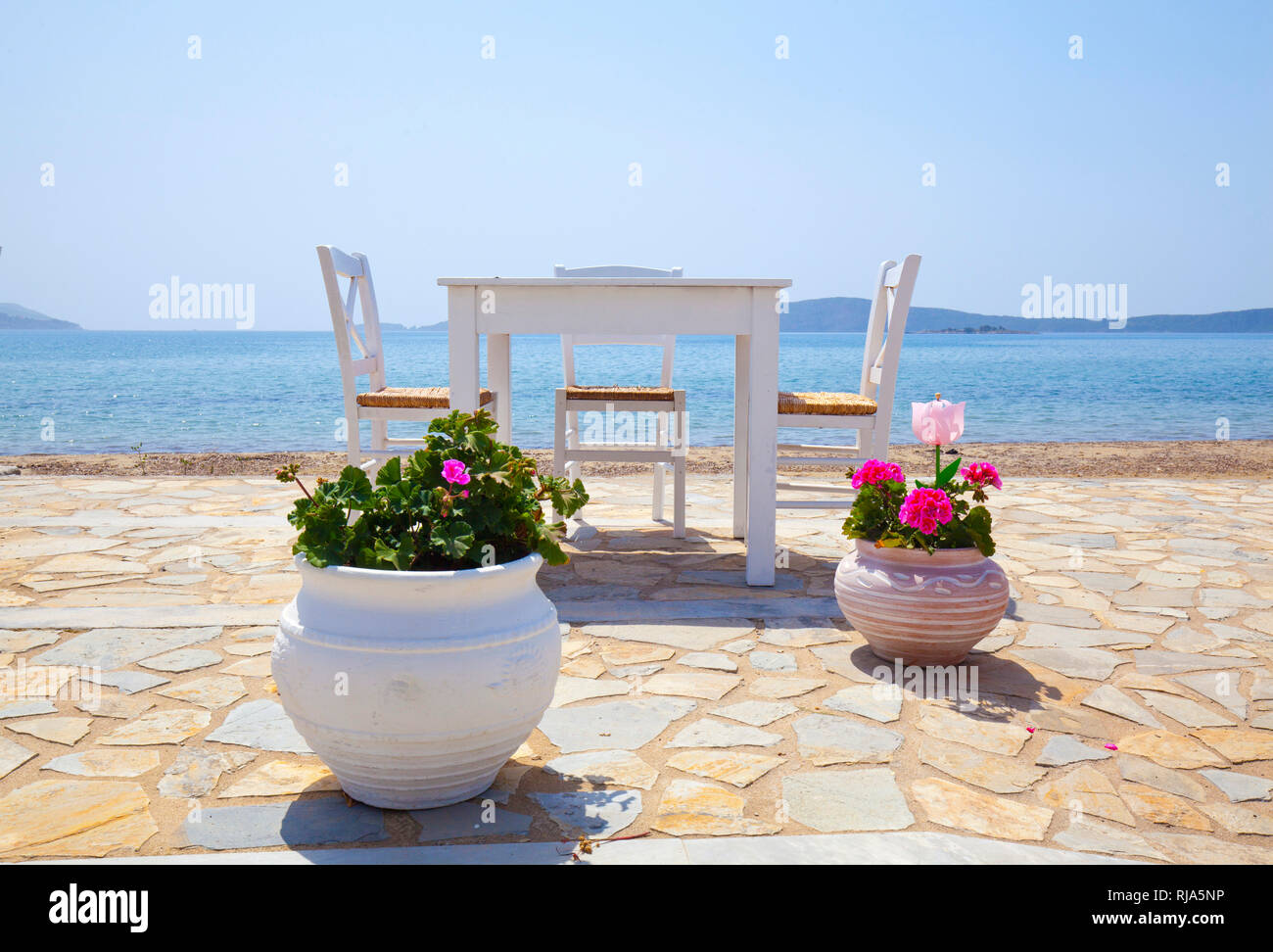 Decorative flower tub on terrace with white table and chairs by the sea ...