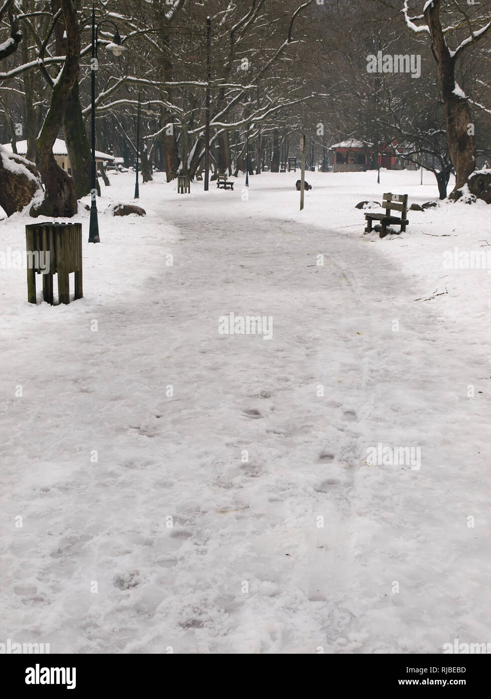 Snow covered Agios Nikolaos (Saint Nicholas) park with benches and path ...