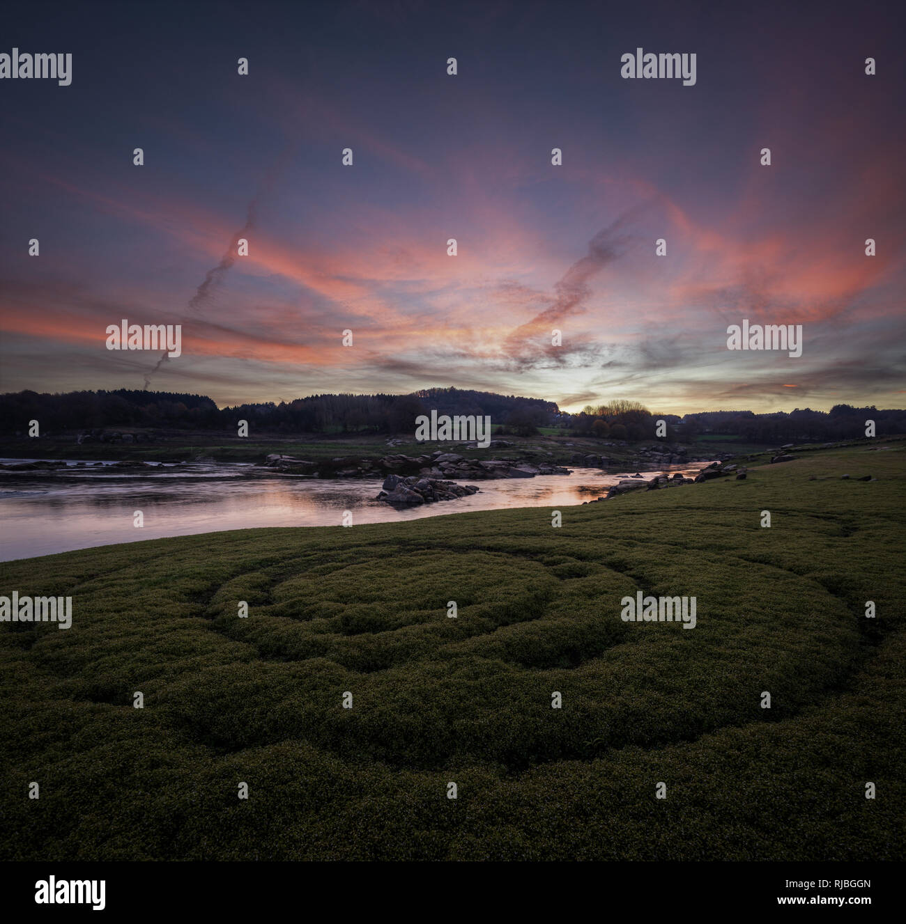 Golden sunset over a river, with a spiral in the grass in the ...