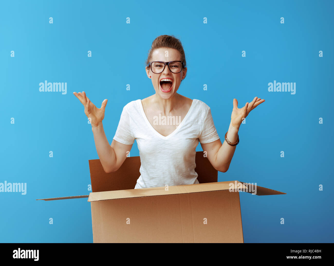 happy modern woman in white t-shirt pops out of a cardboard box ...