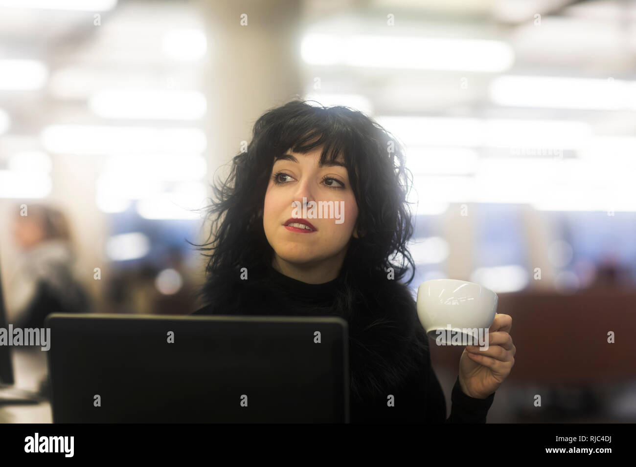 Businesswoman sitting in front of a computer screen drinking a cup of ...