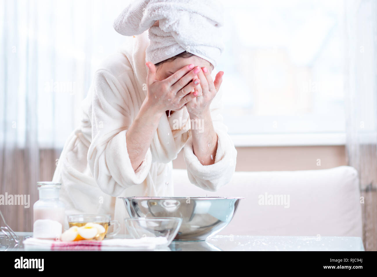 Beautiful young woman with a towel on her head washing her face with ...