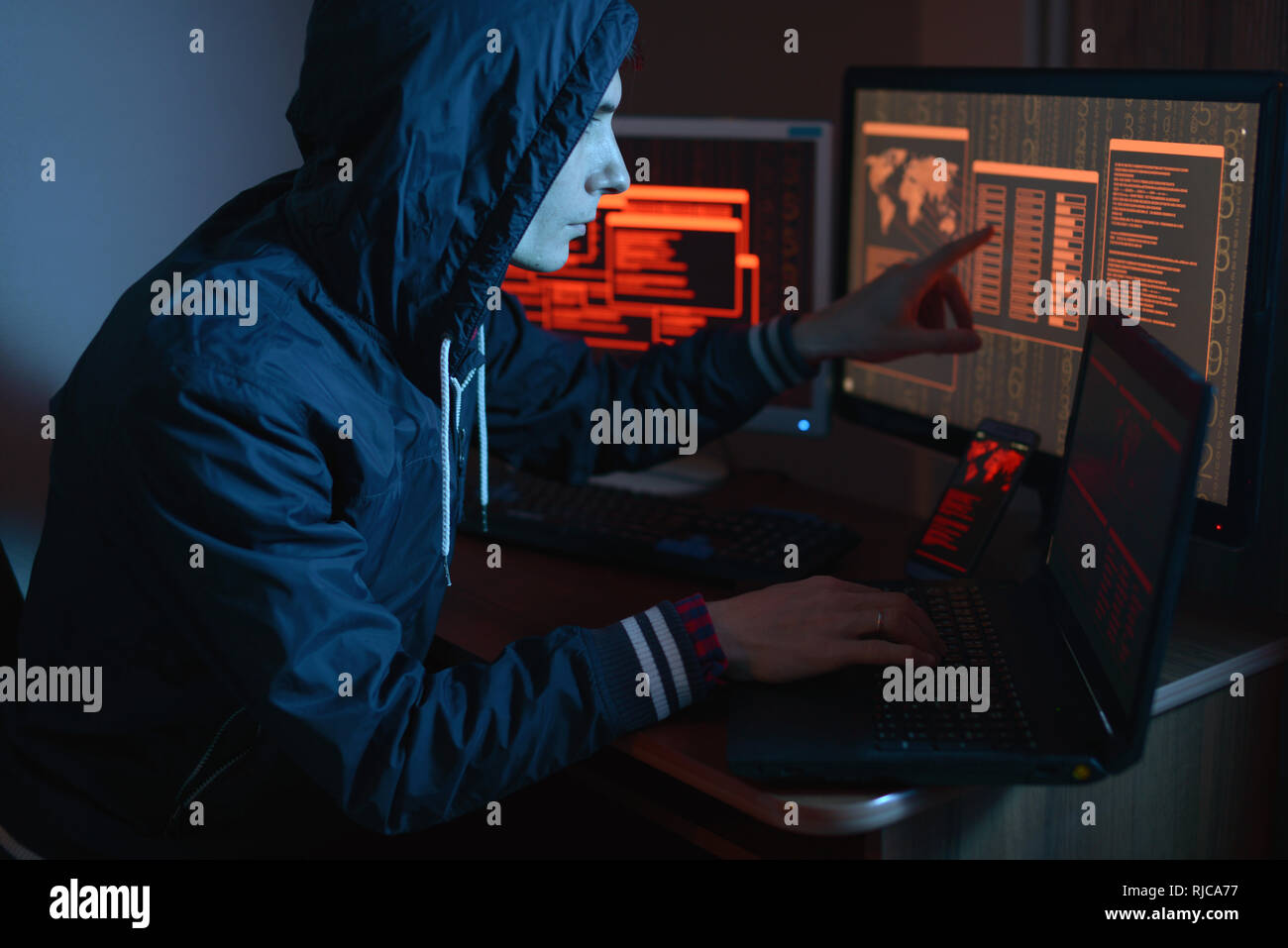 The male hacker in the hood is pointing his finger at the display ...