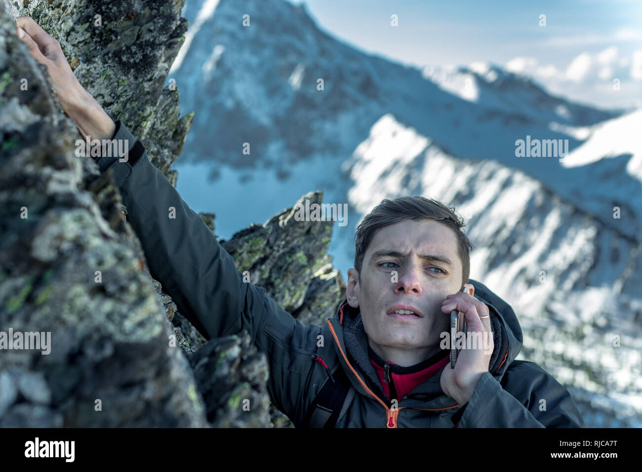 A young man climbing the mountain to the top and talking on the phone ...