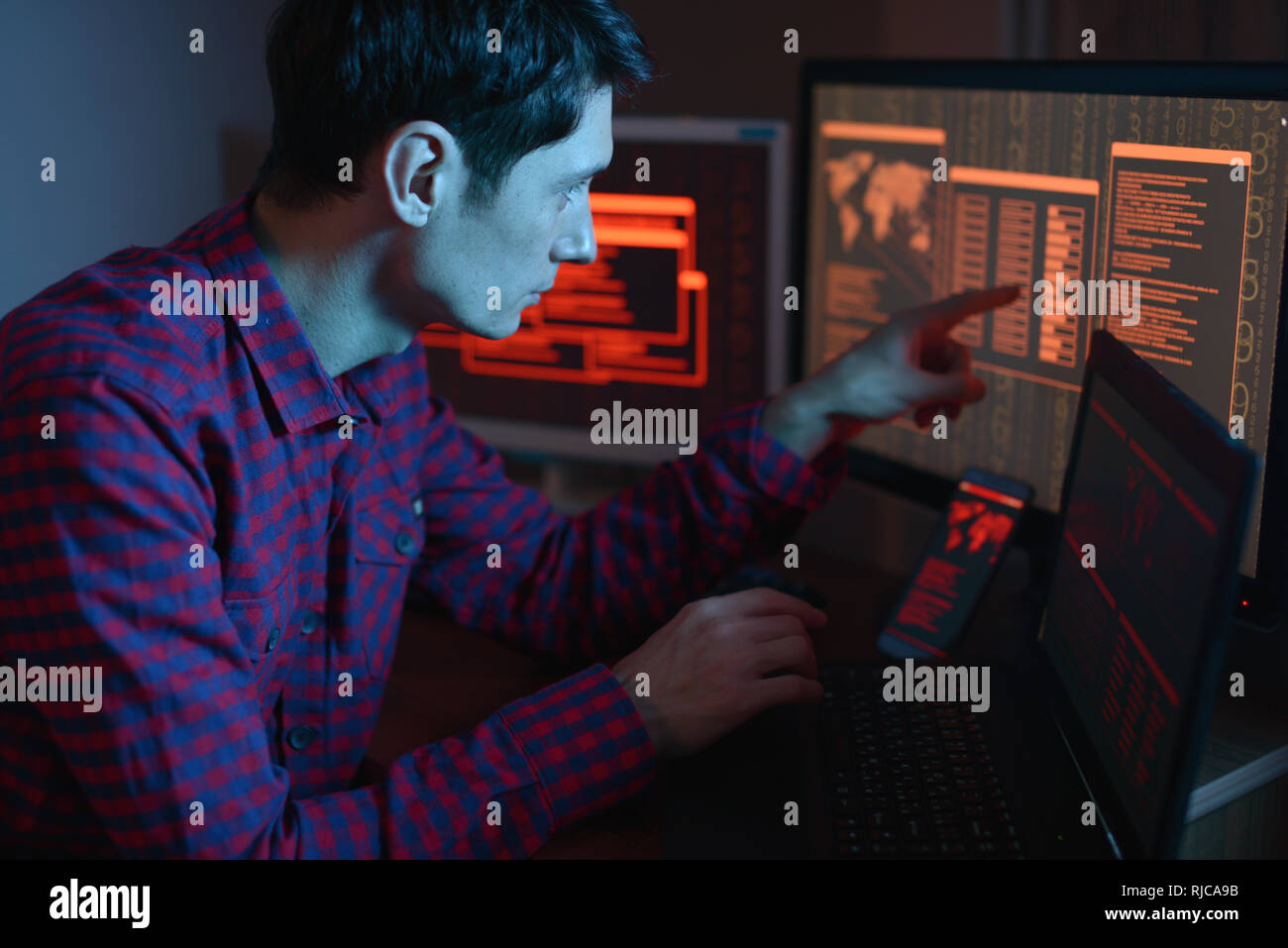 The male hacker in the hood is pointing his finger at the display ...