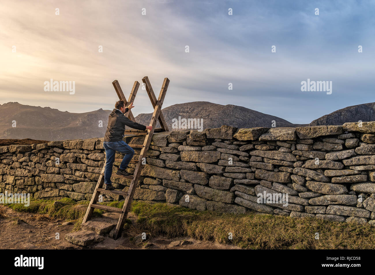Middle age man climbing a ladder on the stone wall in mountains ...