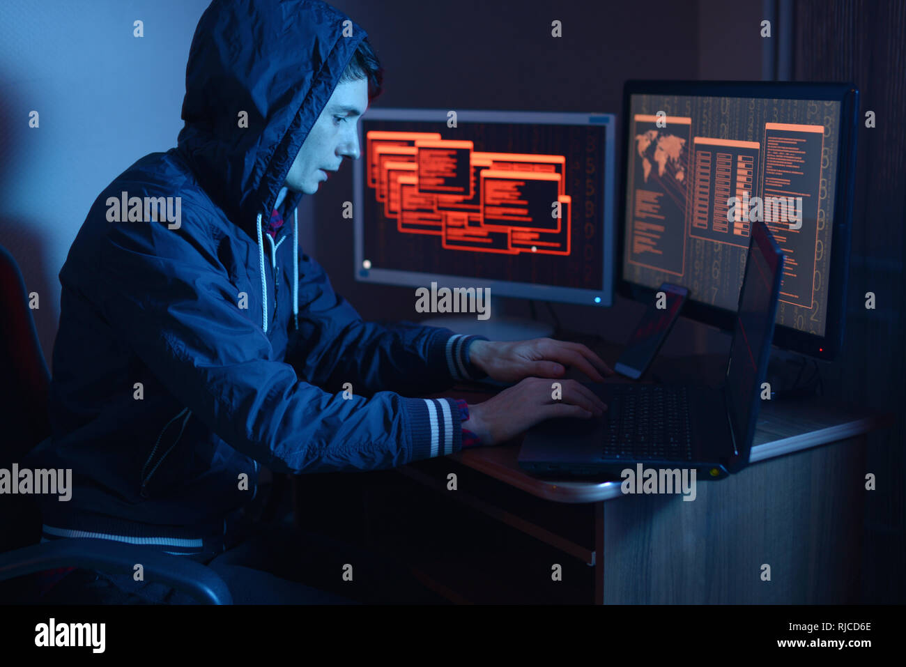 A Male Hacker In A Hood Typing Program Code While Committing A