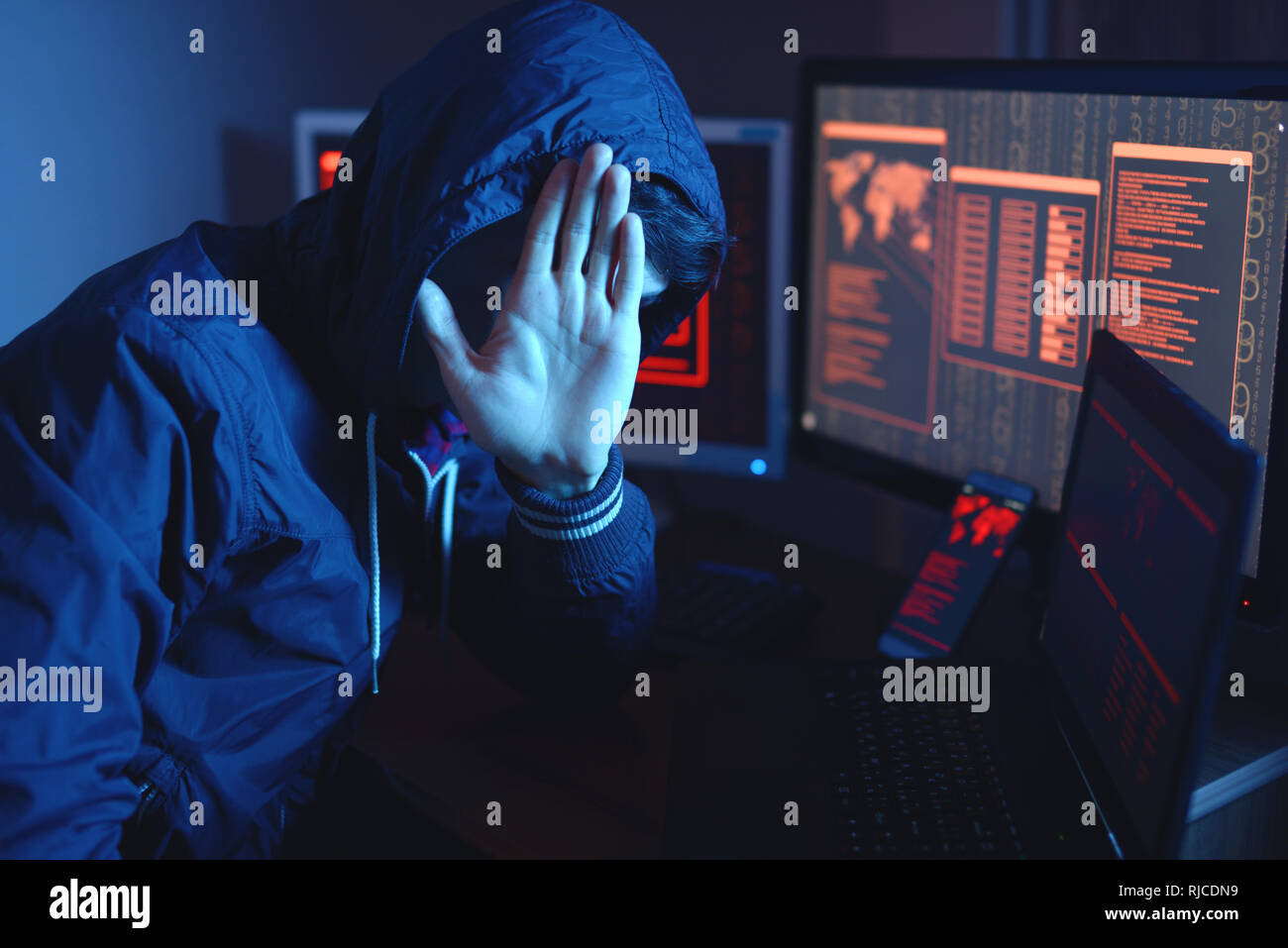 An anonymous male hacker covers his face with hand while committing a ...