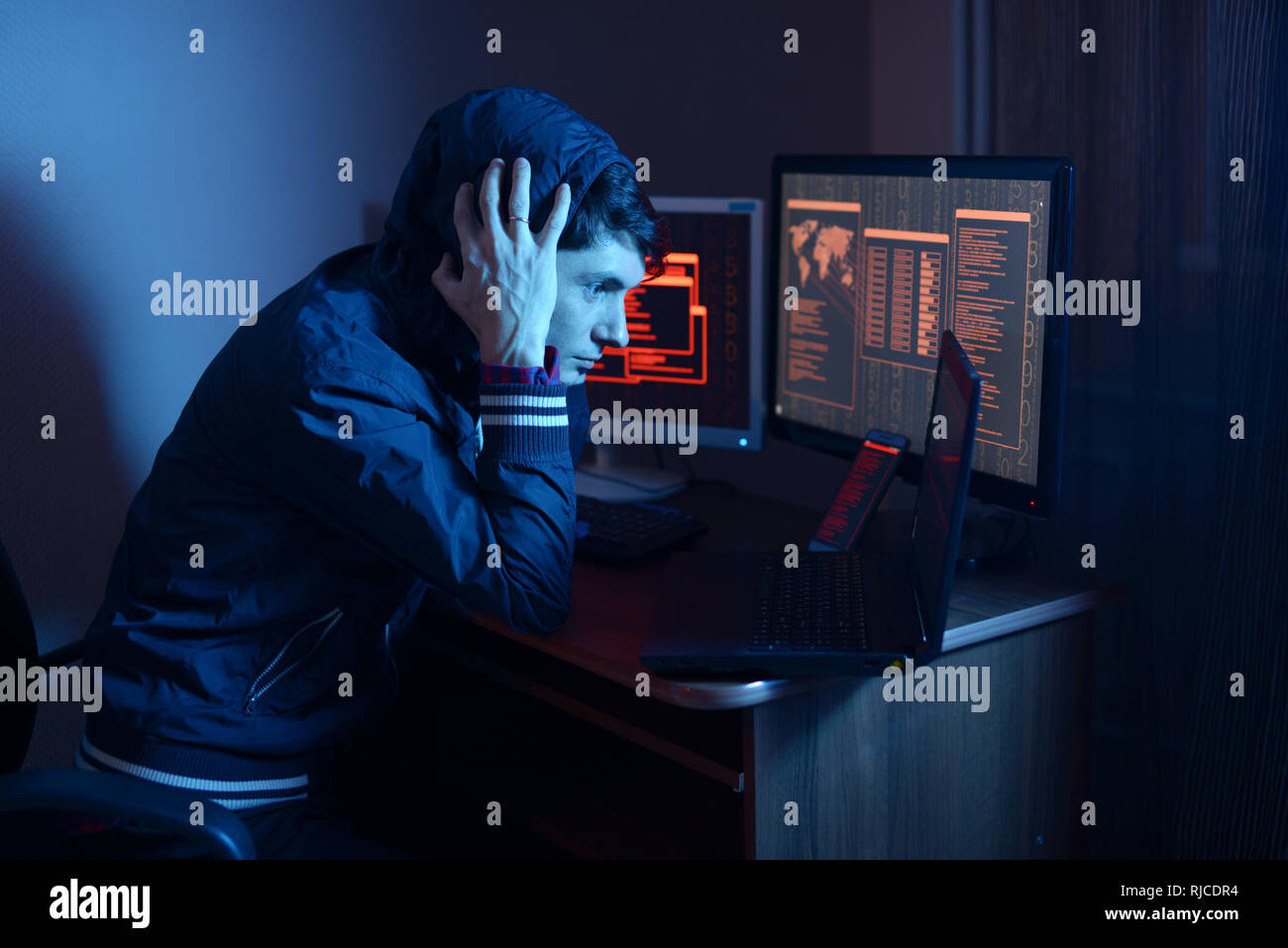 A male hacker in a hood thinking about the problem of hacking or ...
