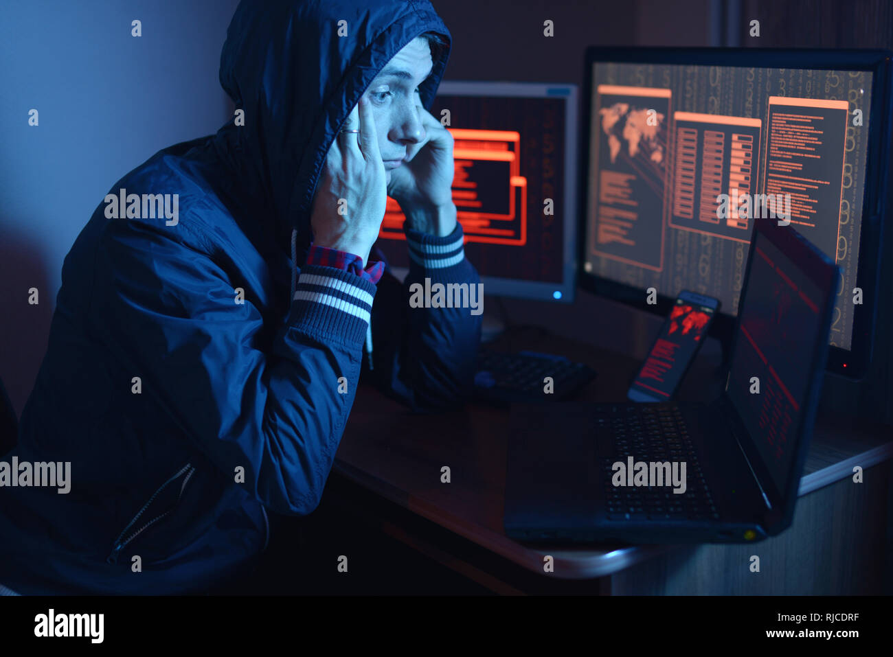 A male hacker in a hood thinking about the problem of hacking or malware infection on the ...