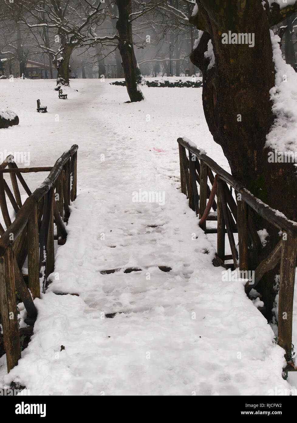 Snow covered Agios Nikolaos (Saint Nicholas) park with benches and path ...