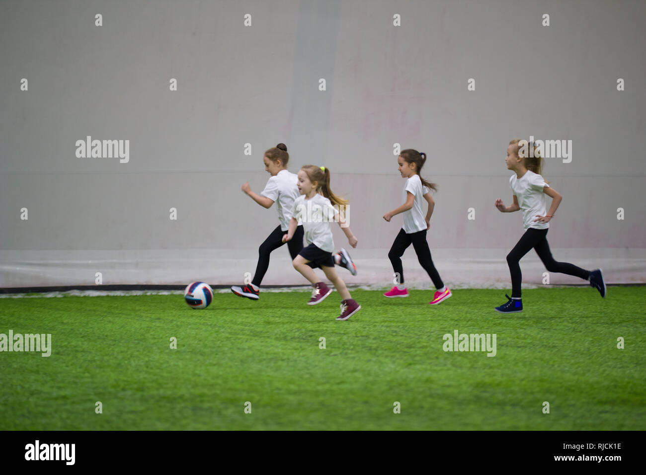 Children playing football indoors. An excited little girls following ...