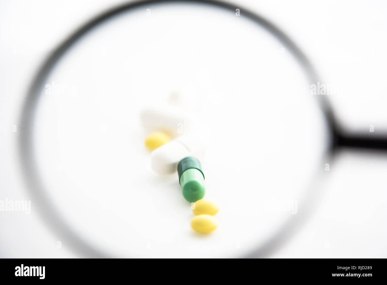 Hand holding magnifying glass focus on assorted colorful pills and ...