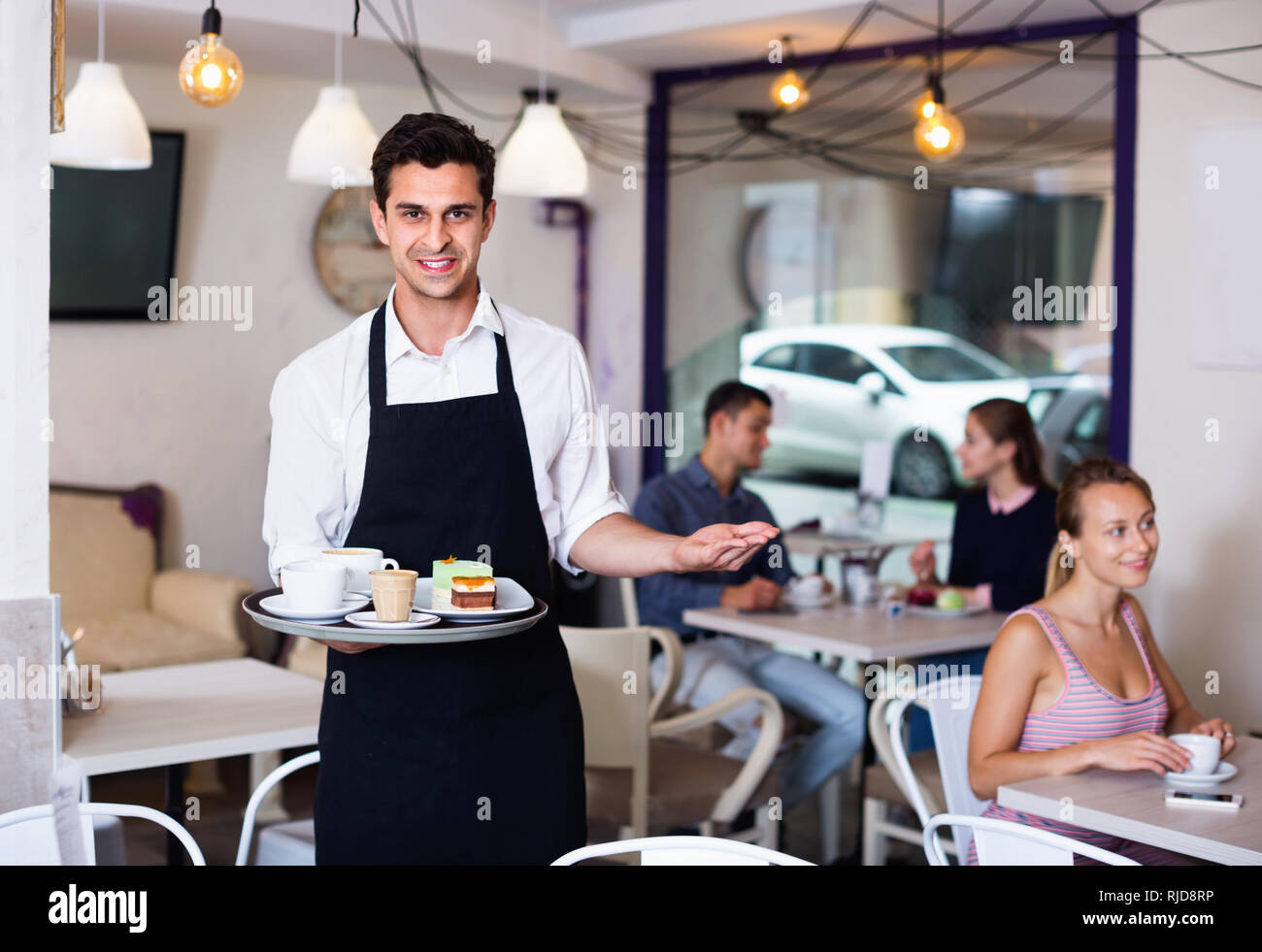 Positive smiling waiter holding served tray meeting visitors at pastry ...