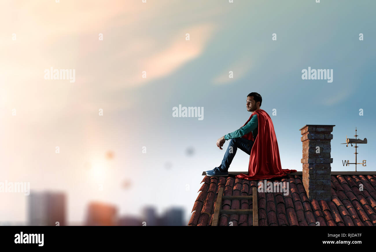 Thoughtful man in cape sitting on top of building. Mixed media Stock ...