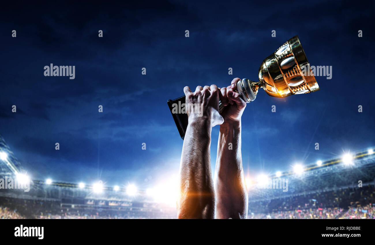 Hand of athlete holding cup trophy against stadium. Mixed media Stock ...