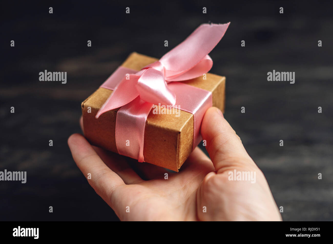 Hand holding Holiday gift box Packed in crafting paper with pink ribbon ...