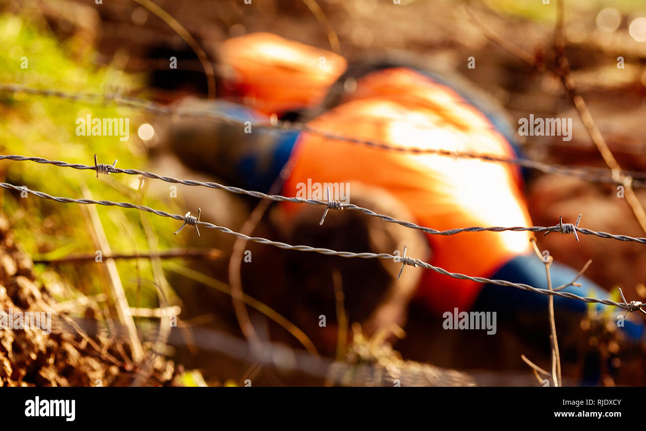 Unfocused of a mud race runners passing under a barbed wire obstacles ...