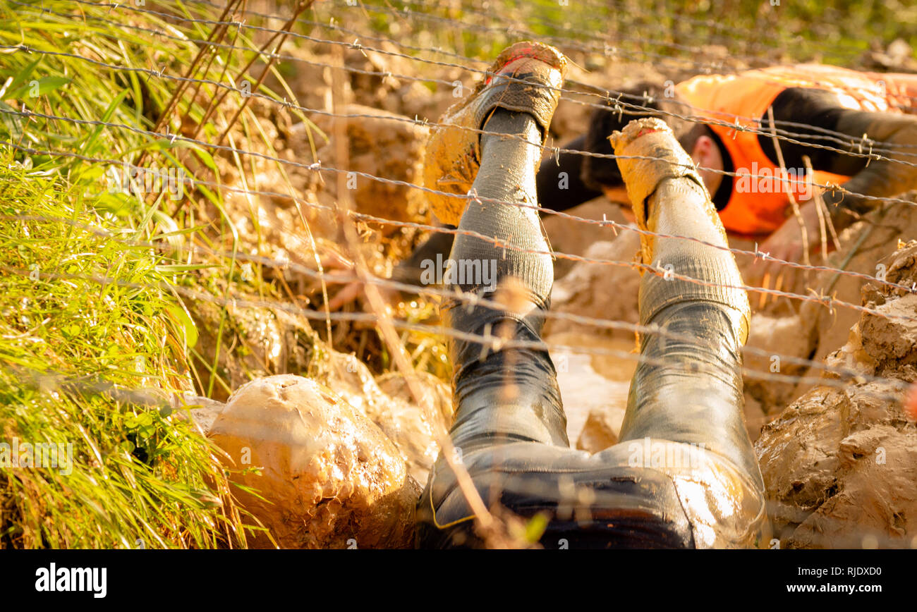 Trail running athlete crossing the dirty puddle under a barbed wire in ...