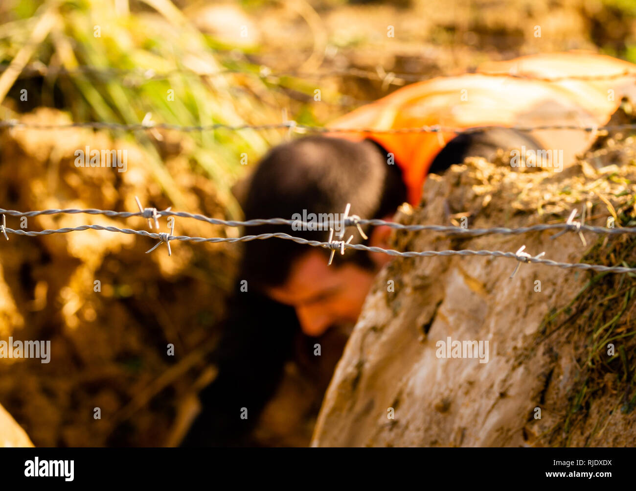 Unfocused of a mud race runners passing under a barbed wire obstacles ...
