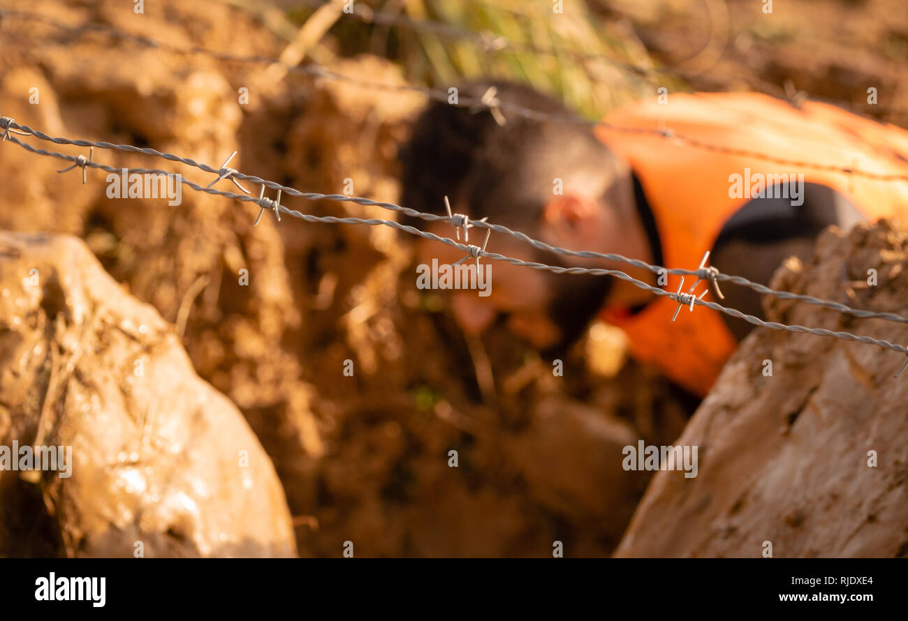 Unfocused of a mud race runners passing under a barbed wire obstacles ...