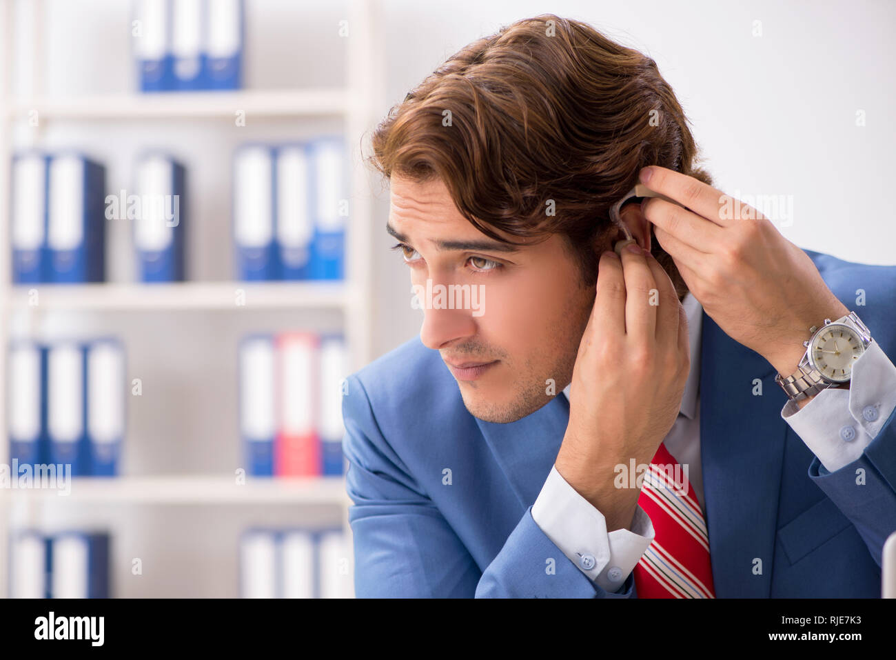 Deaf employee using hearing aid in office Stock Photo - Alamy