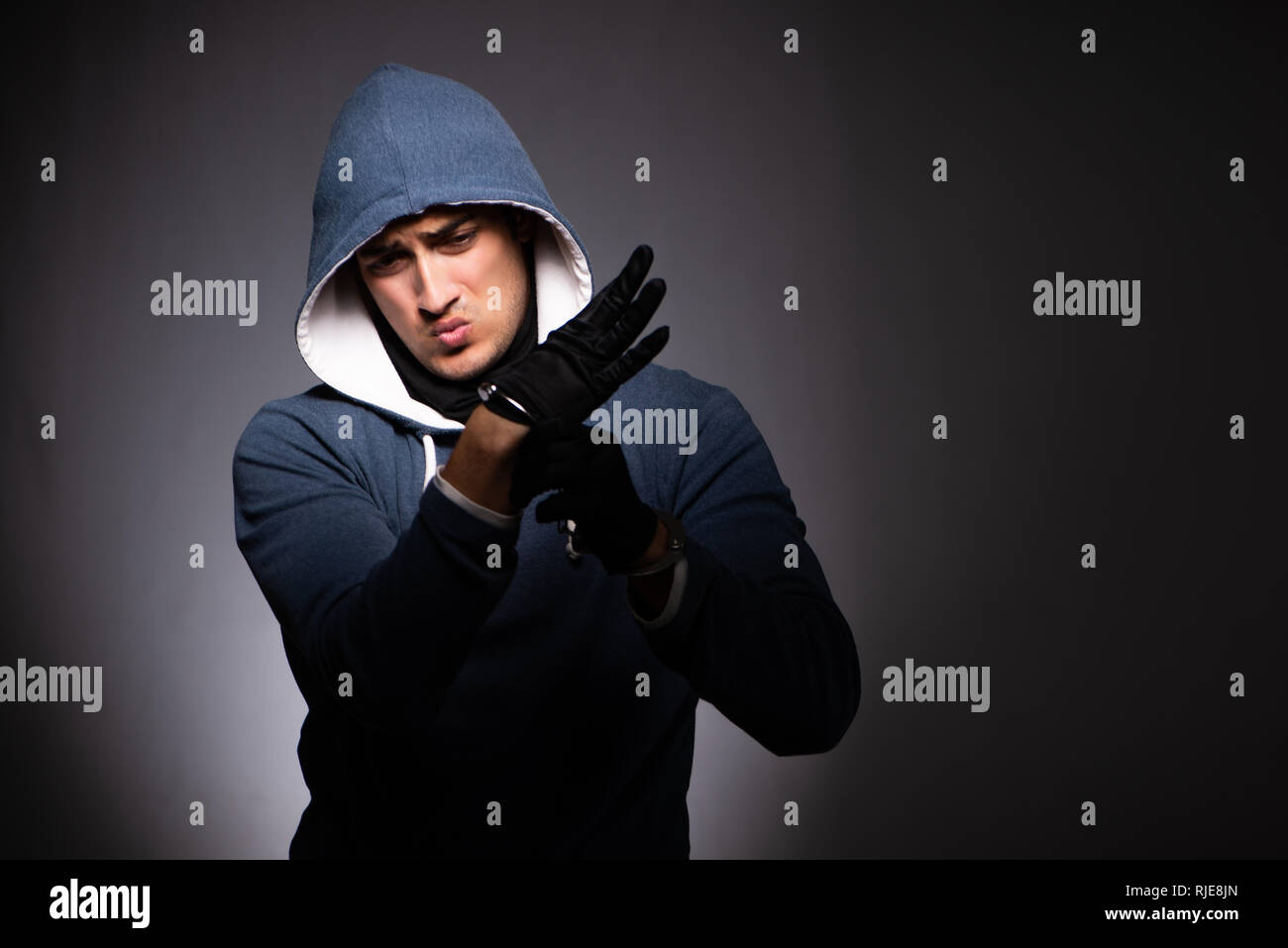 Young gangster in hood on grey background Stock Photo - Alamy