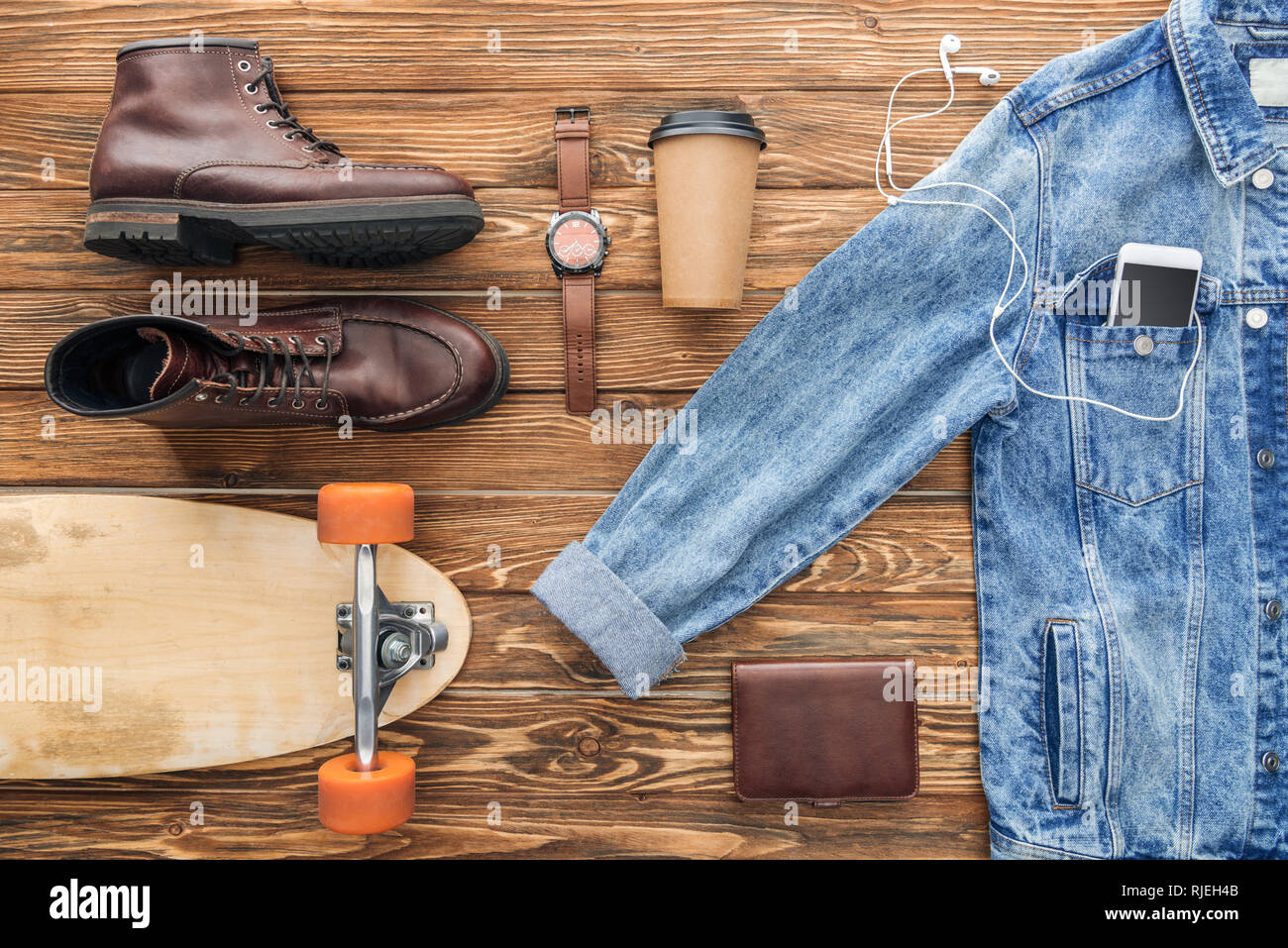 Flat lay with denim jacket, boots and longboard on wooden background ...