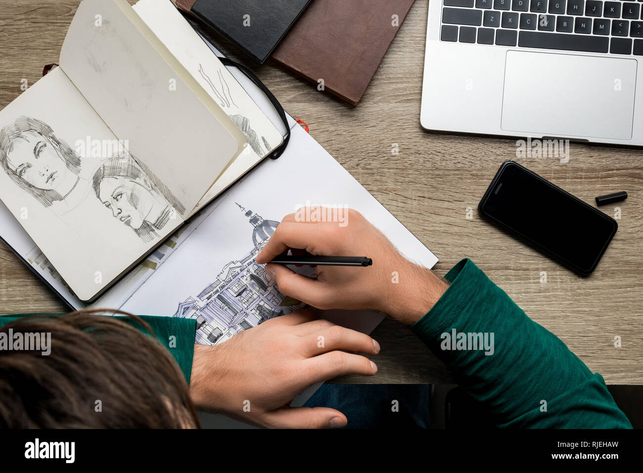 overhead back view of man drawing in album on wooden table next to ...