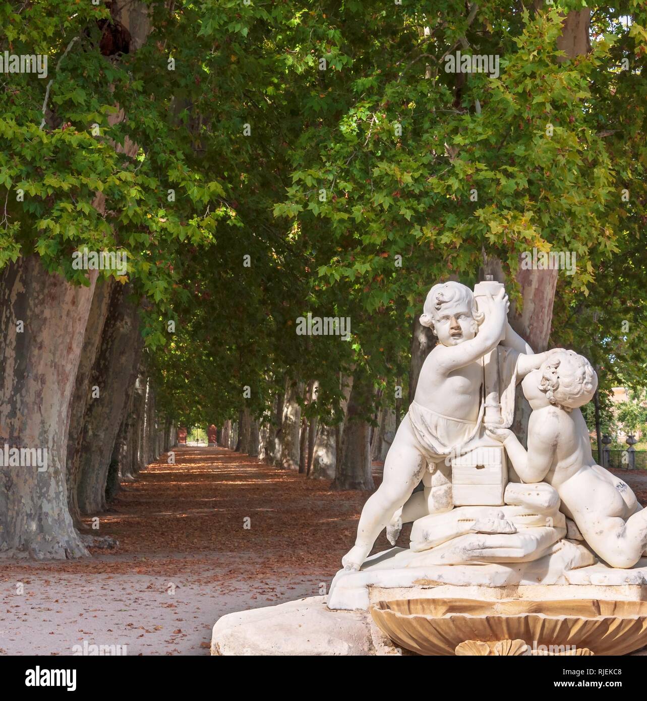 A statue of two figures set in public gardens in front of a leafy ...