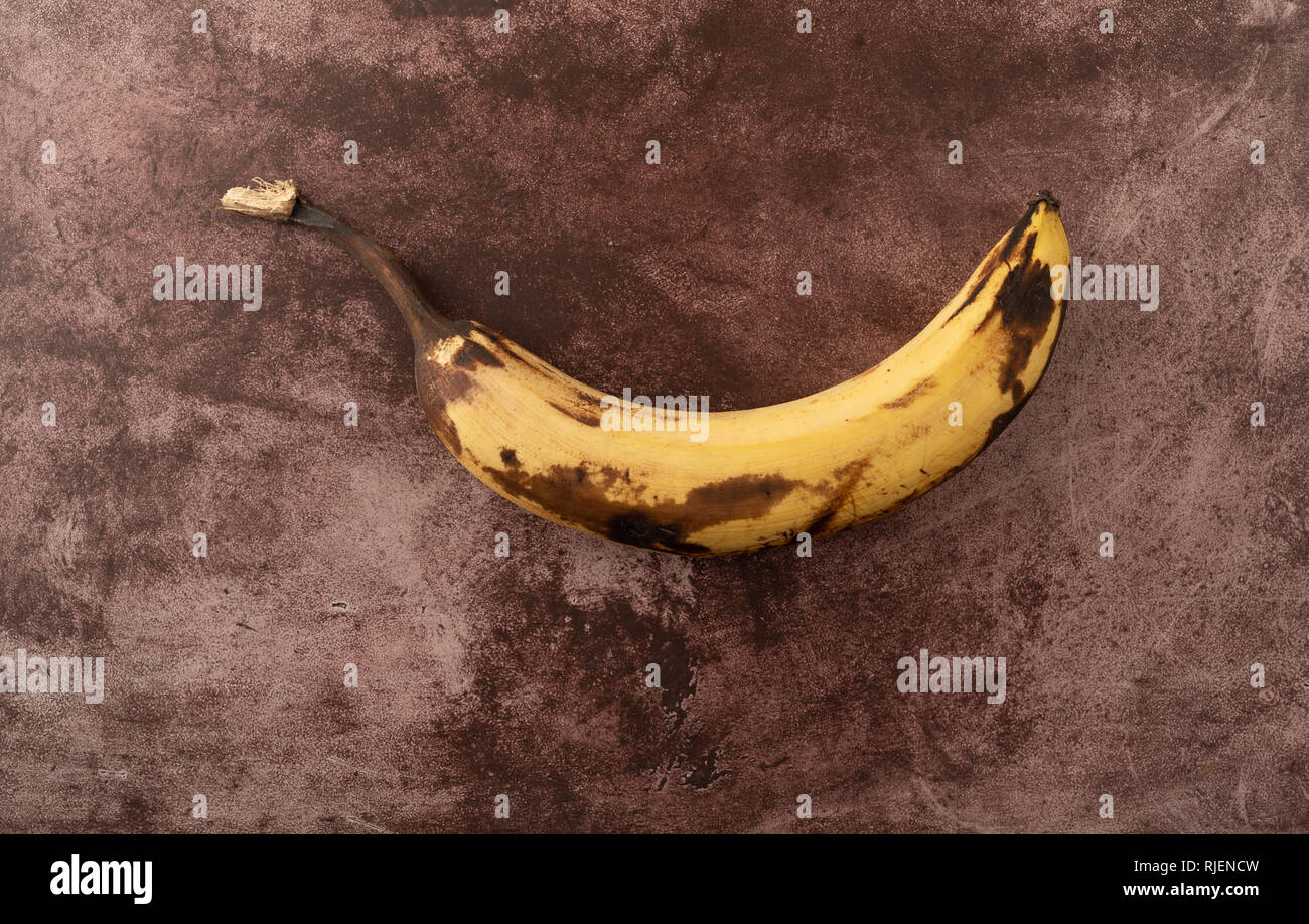 Overhead view of a single overripe yellow banana on a maroon counter ...