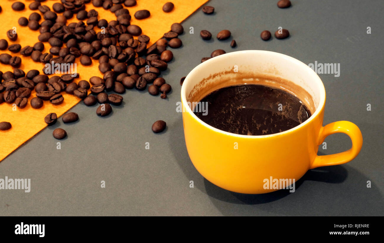 Yellow cup of coffee on a gray and yellow background with coffee beans ...