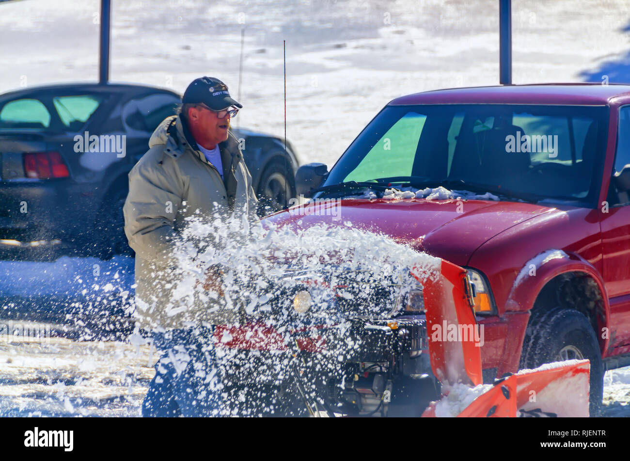 A man clearing thawing snow from a sidewalk with a snow blower after a ...