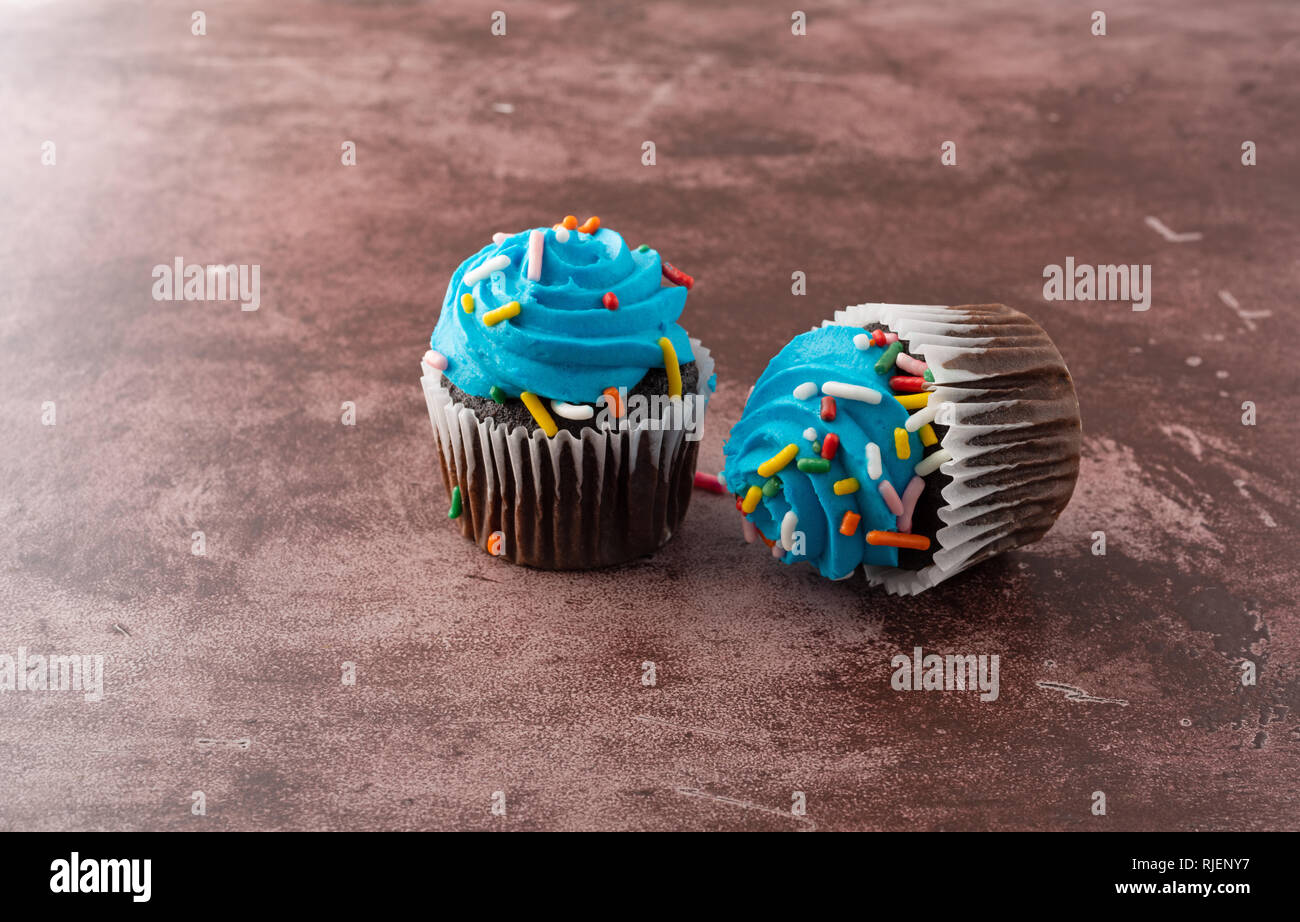 Side view of two blue frosted chocolate cupcakes with one tipped over ...