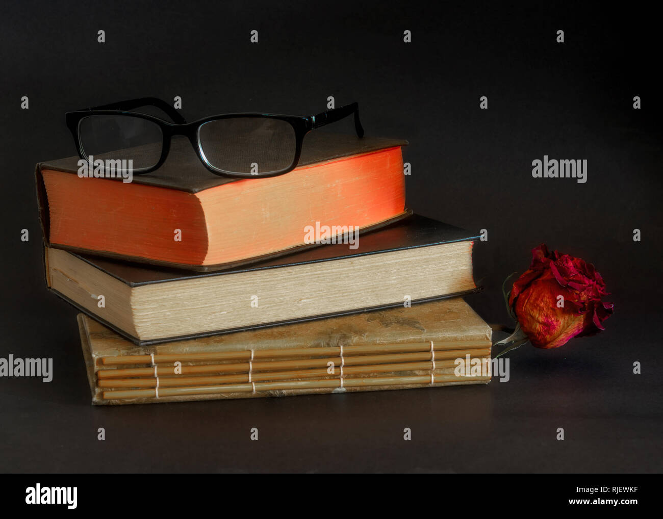 Reading Glasses On Top Of Three Old Books Stacked On Top Of Each Other Against Dark Background