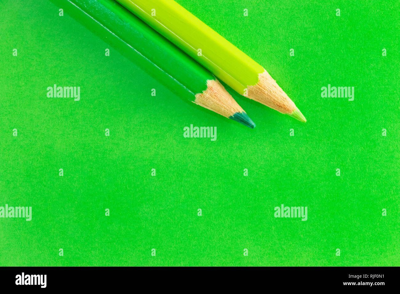 Two green pencils on a colored background , light green and dark green ...