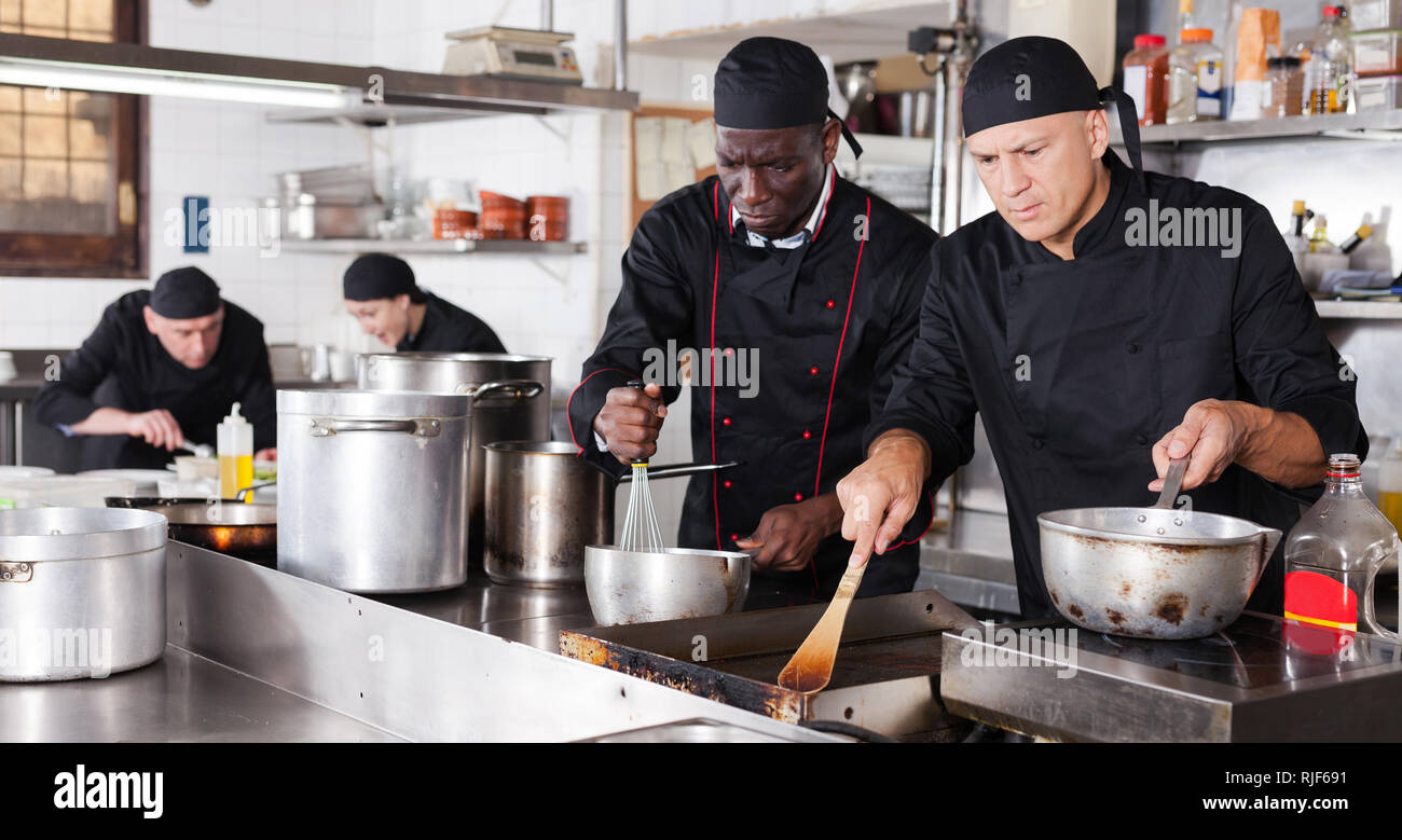 Positive cooks in process of working in kitchen of restaurant Stock ...